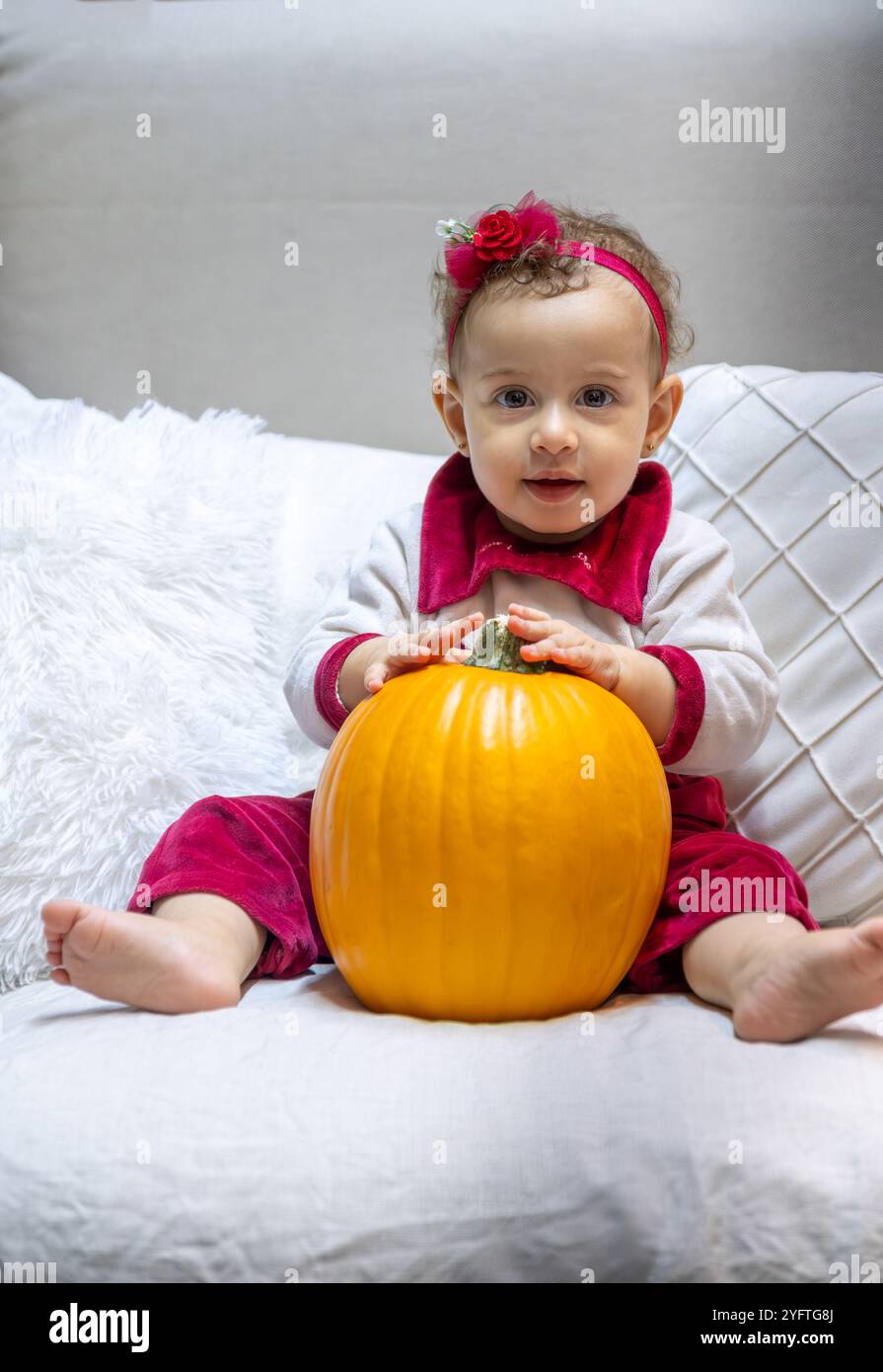A cheerful baby wearing a red outfit with a headband, sitting on a ...