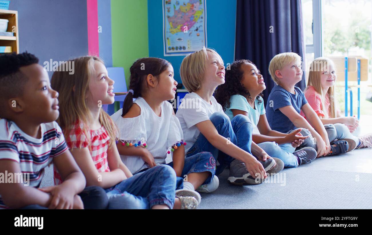 Group Of Smiling Elementary School Pupils Sitting On Floor In A Line ...
