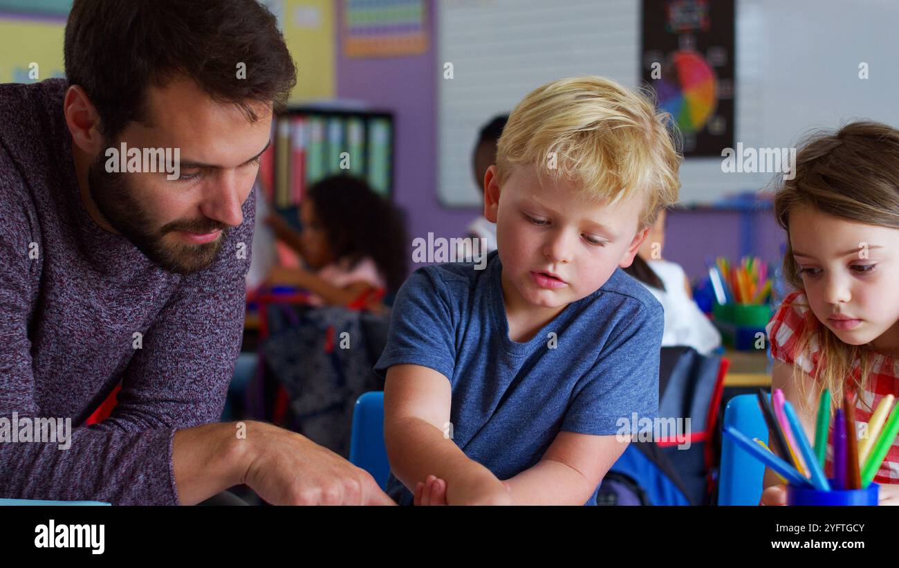 Male Elementary School Teacher Giving Male Pupil One To One Support In ...