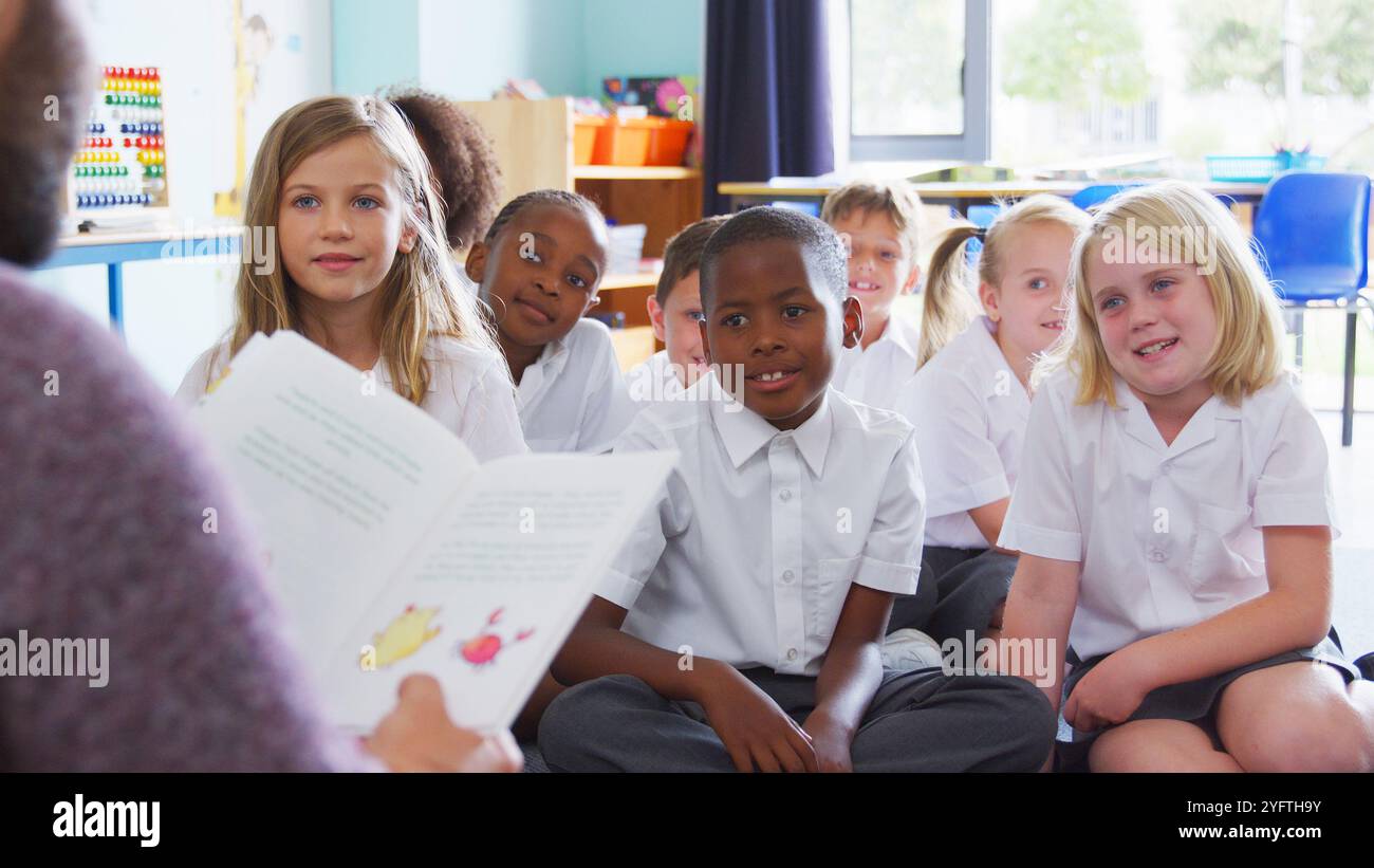 Male Teacher Reading Story To Group Of Elementary Pupils Wearing ...