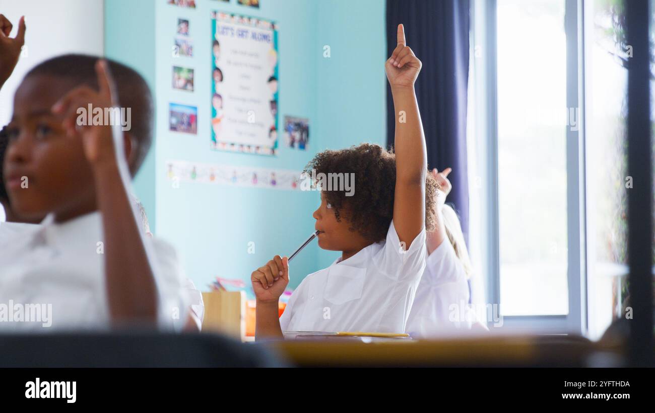 Group Of Uniformed Elementary Pupils In School Classroom Raising Hands ...