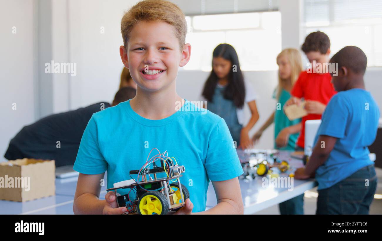 Portrait Of Smiling Male Student Holding Robot Vehicle Built In School ...
