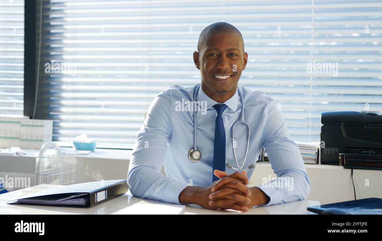Portrait Of Smiling Male Doctor Wearing Stethoscope Sitting Behind Desk ...