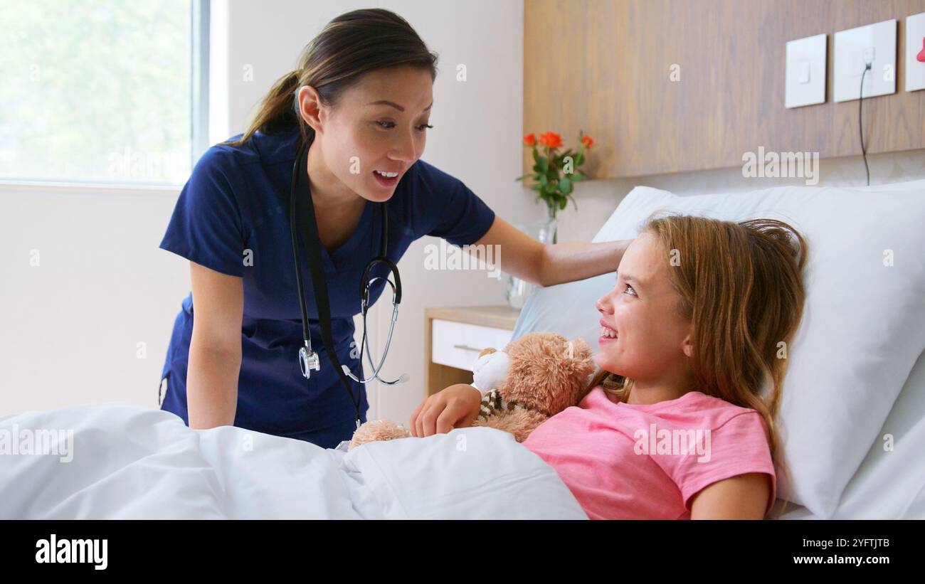 Female Nurse Wearing Scrubs Visiting Girl Patient Lying In Hospital Bed ...