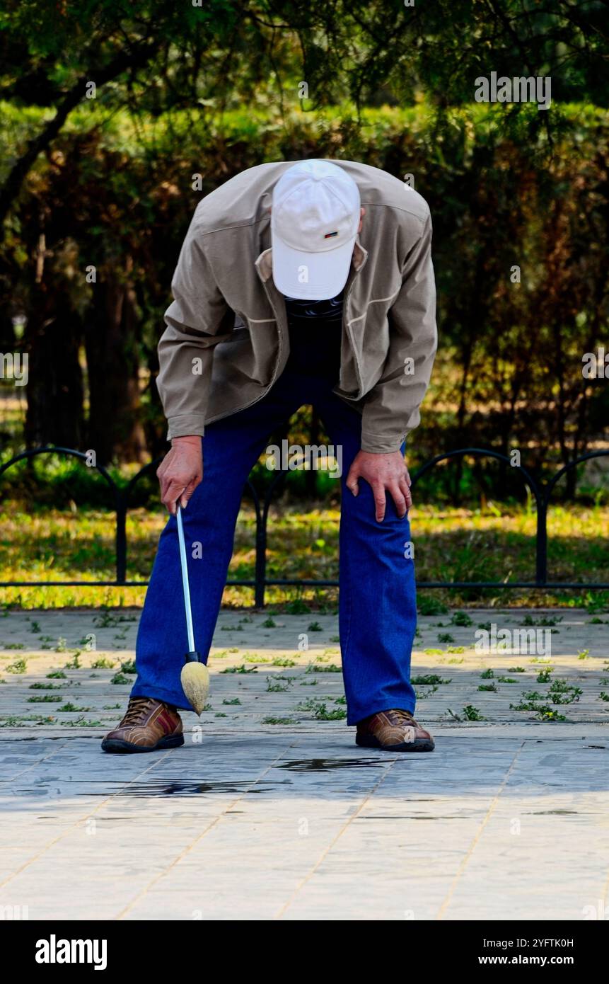 A Chinese man practising calligraphy using water on the pavement in the ...