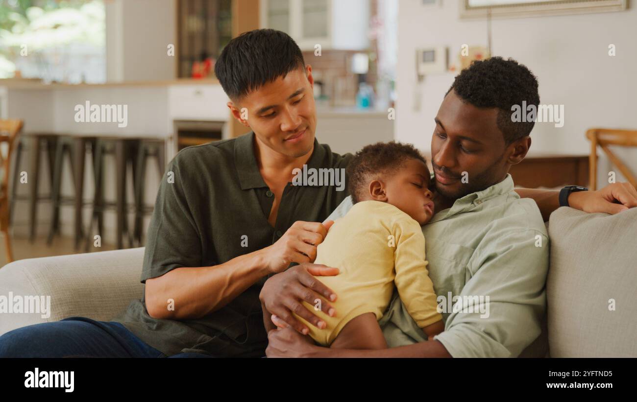 In a warm and inviting living room, two adults nurture a young child peacefully resting in one ...