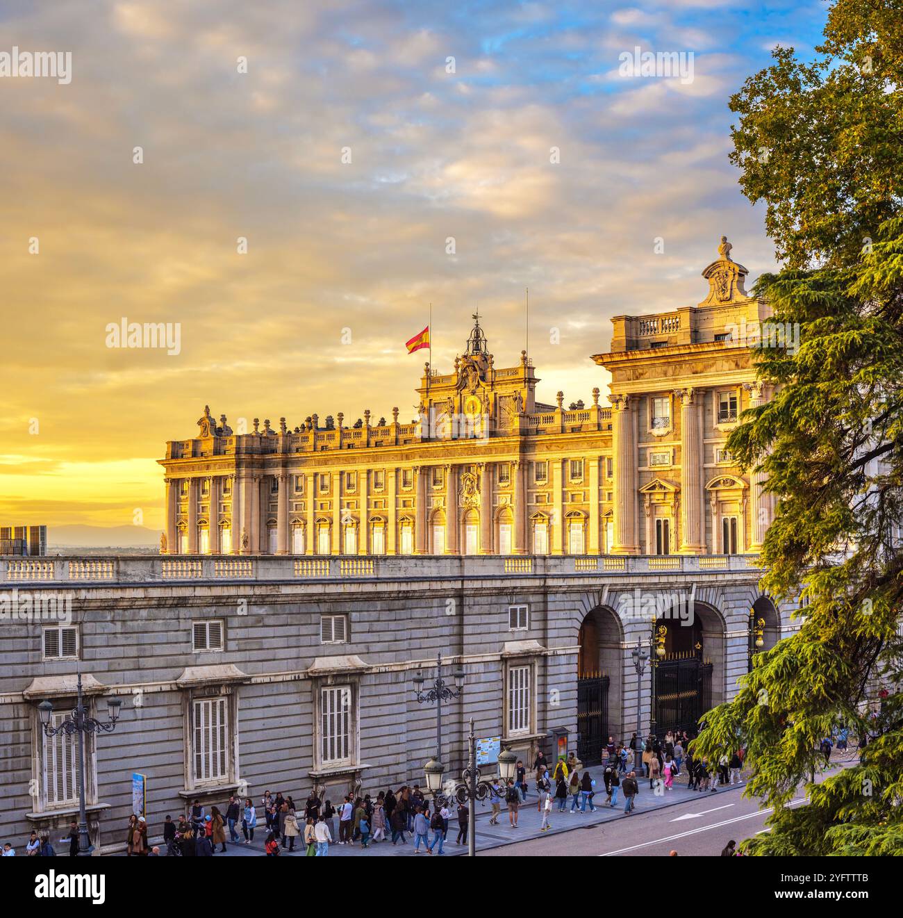 Main facade of the Royal Palace of Madrid at sunset. Tourists gather in ...