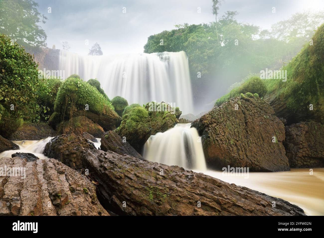 Bottom view of waterfall with yellow water among green woods on ...