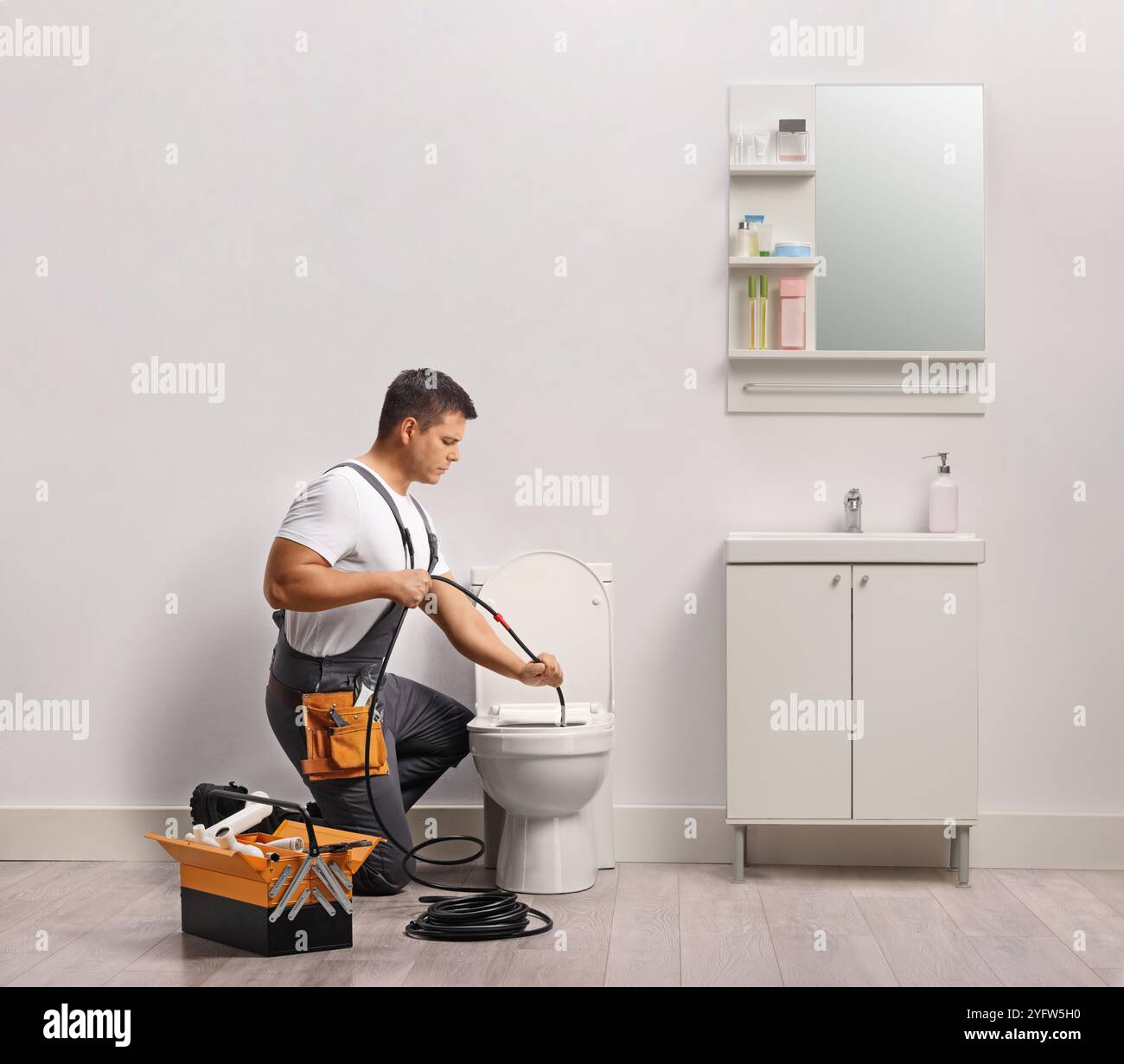 Plumber using a drain snake for clogged toilet in a bathroom Stock ...