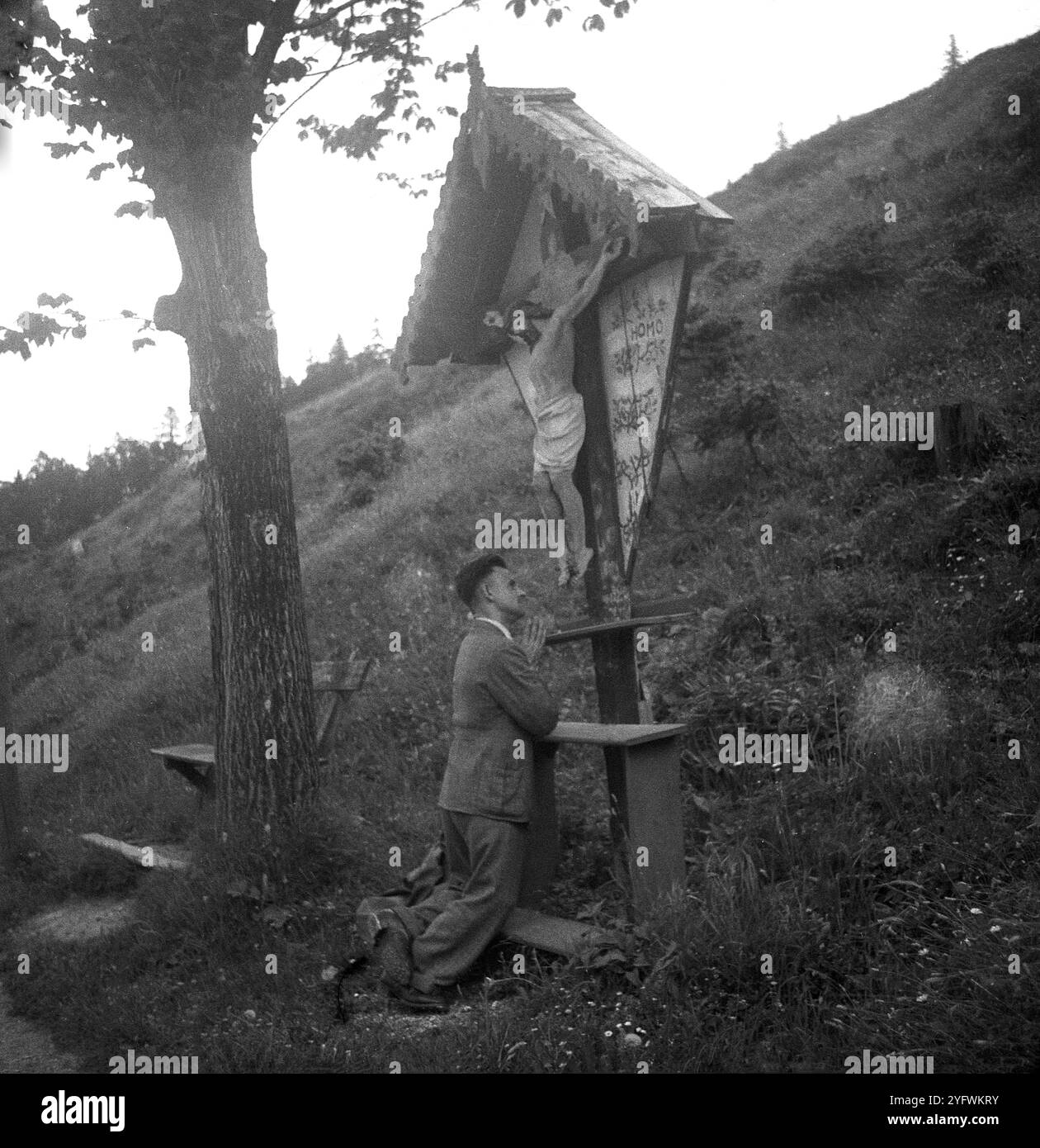 1950s, historical, a man in a suit, kneeling down, hands together ...