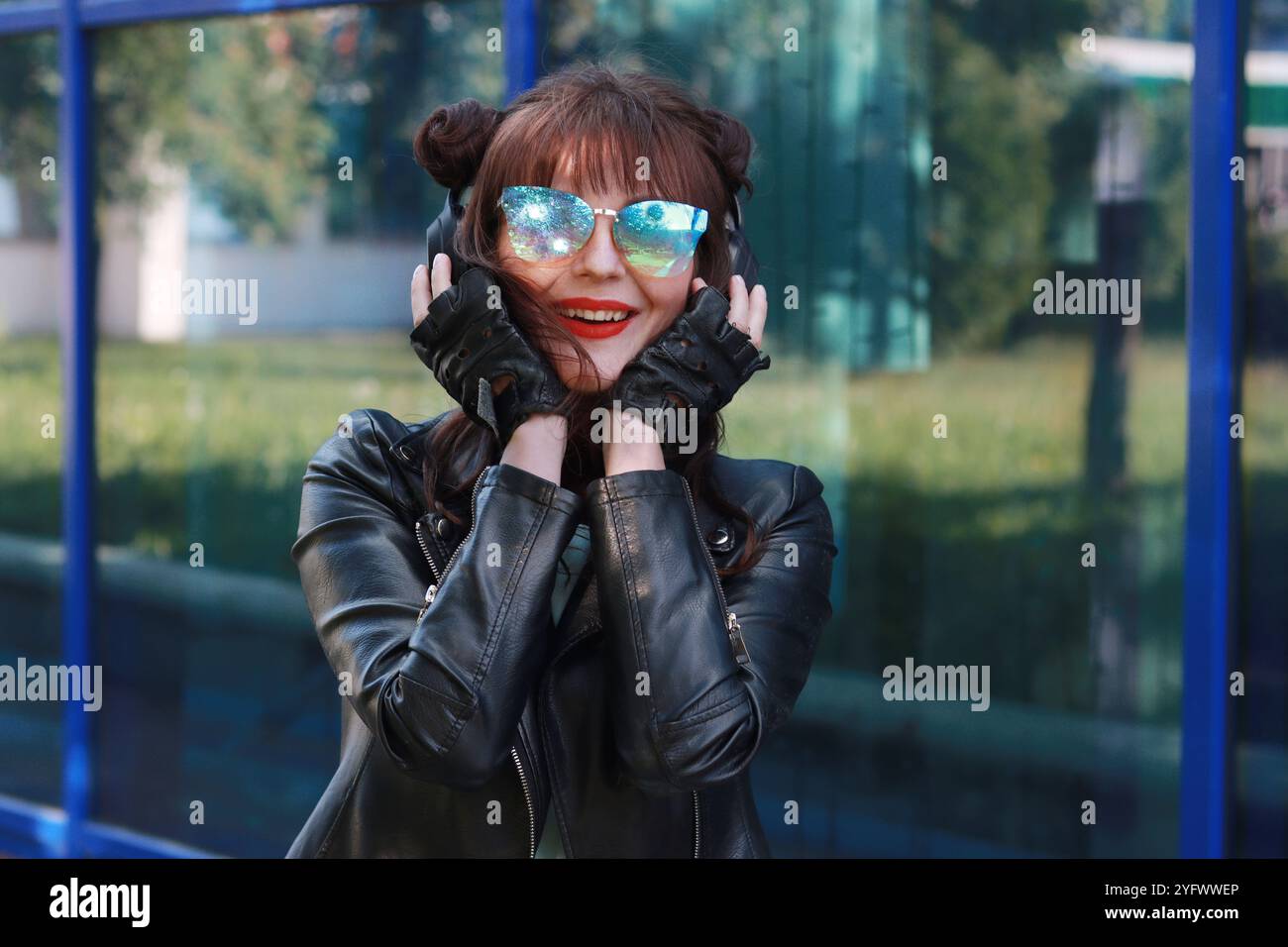 A beautiful girl in a black leather jacket and gloves, wearing blue sunglasses is holding a ...