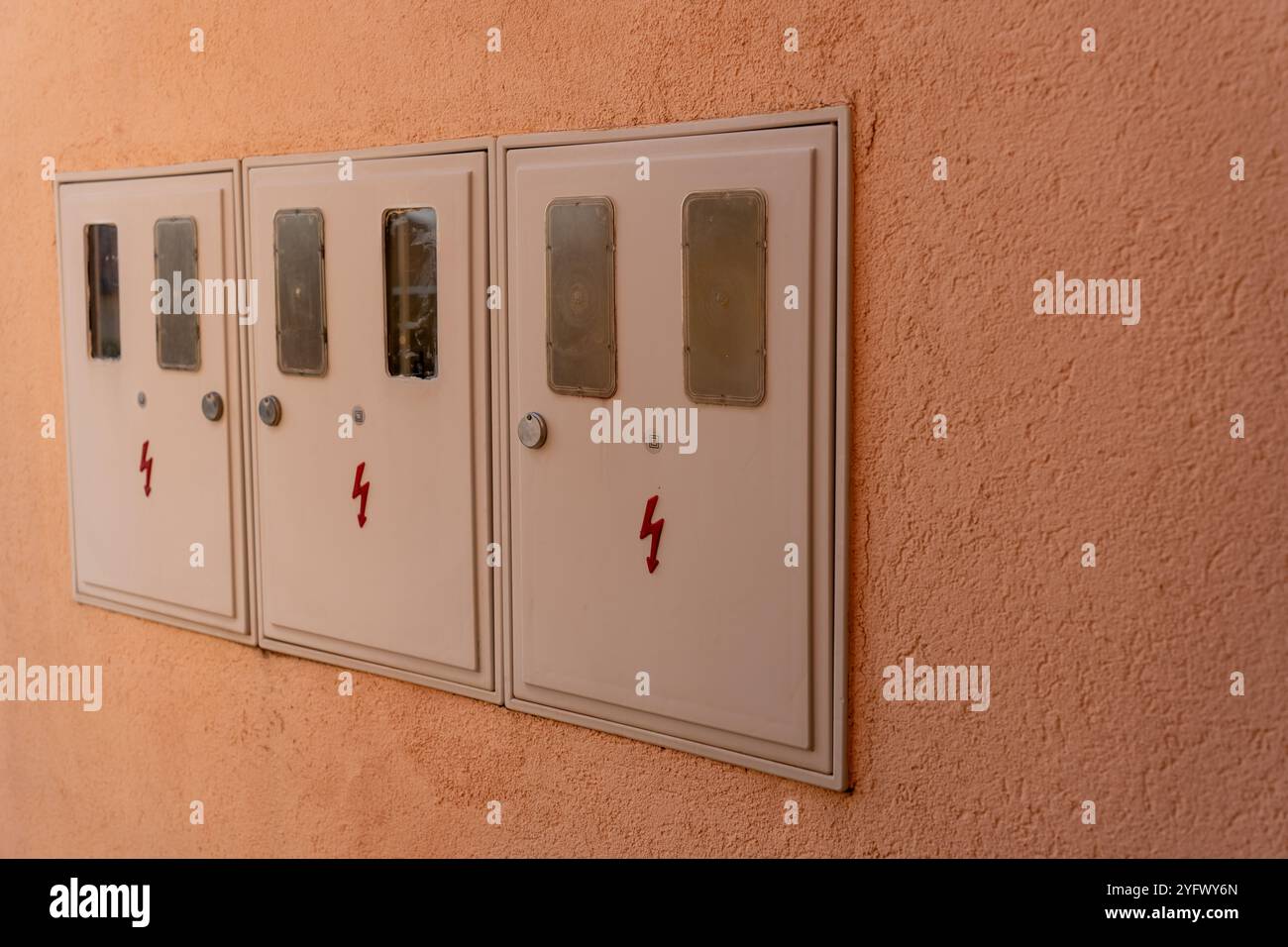 Three electrical meter boxes with warning symbols on textured orange ...