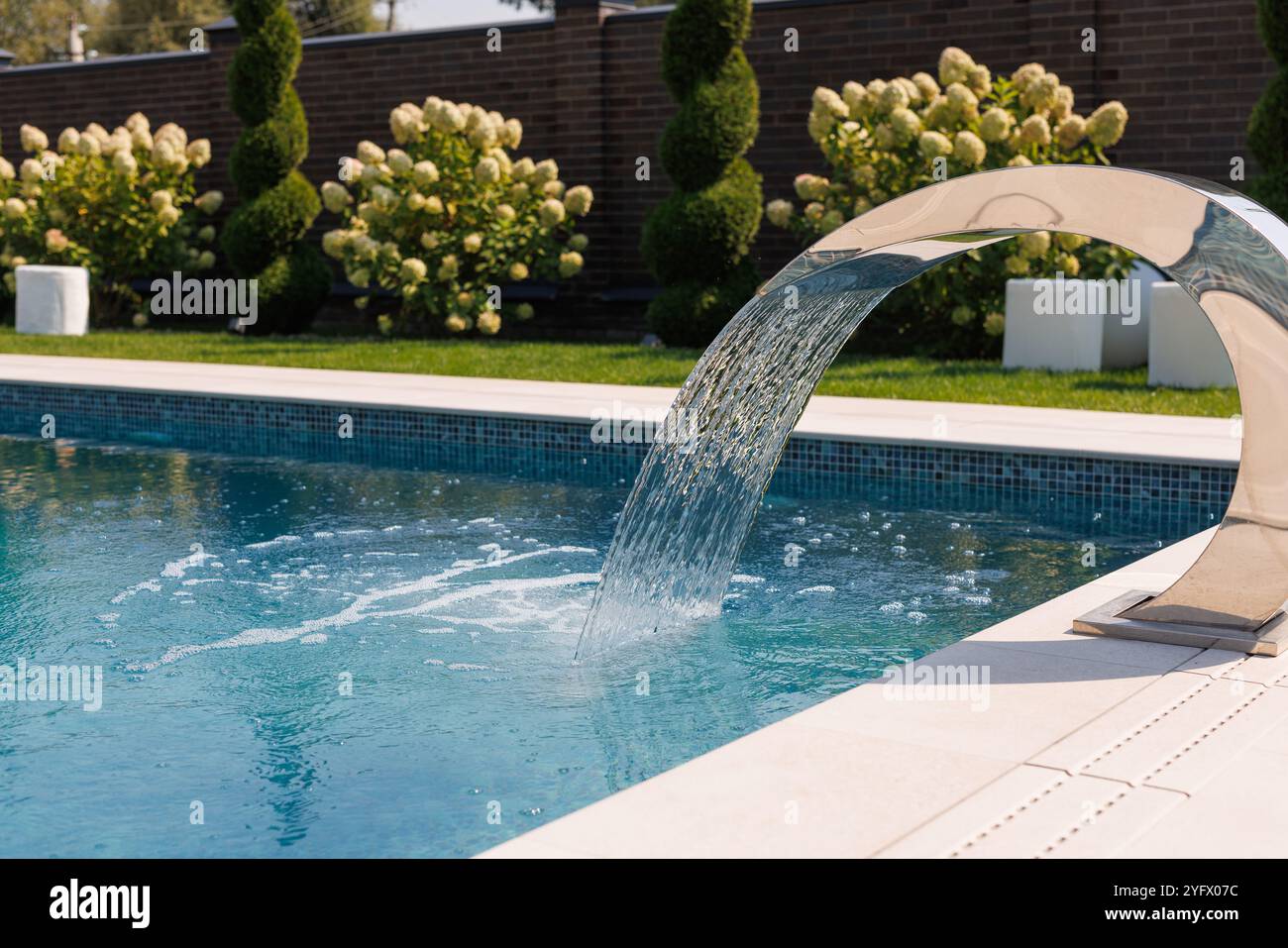 A modern swimming pool with a sleek, curved water feature pouring water ...