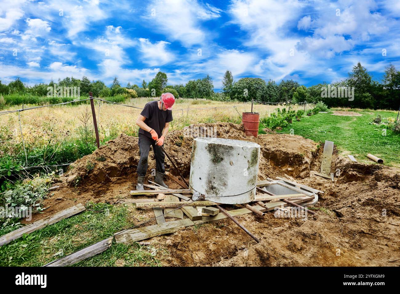 When installing septic tank, worker pushes concrete rings one over ...