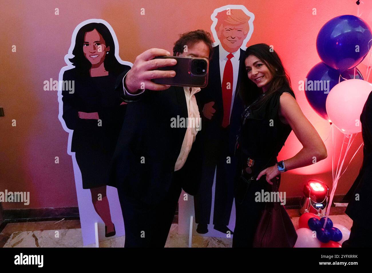 Guests take a selfie with cardboards of Kamala Harris and Donald Trump ...