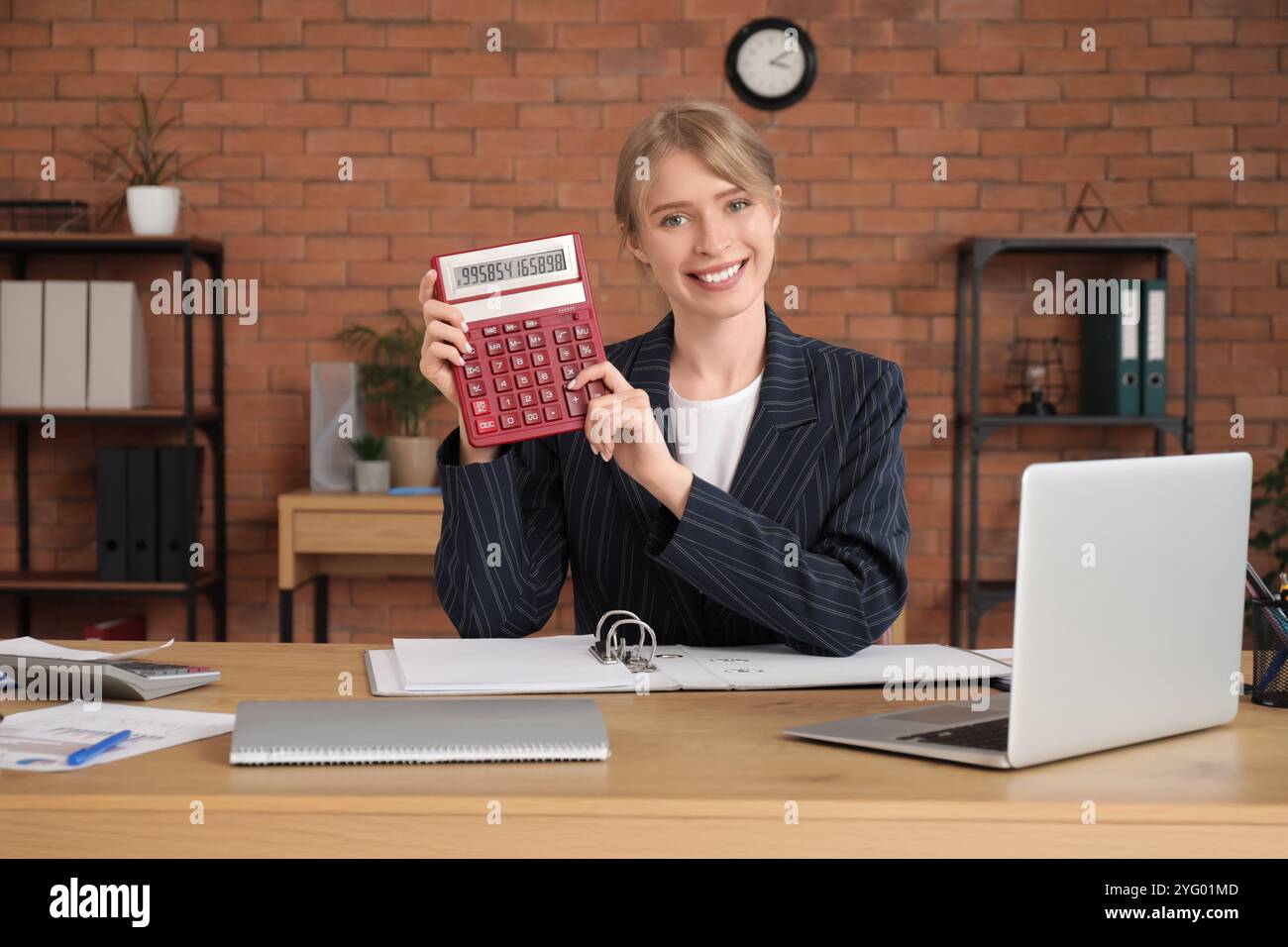 Young shocked female accountant showing calculator at workplace with ...
