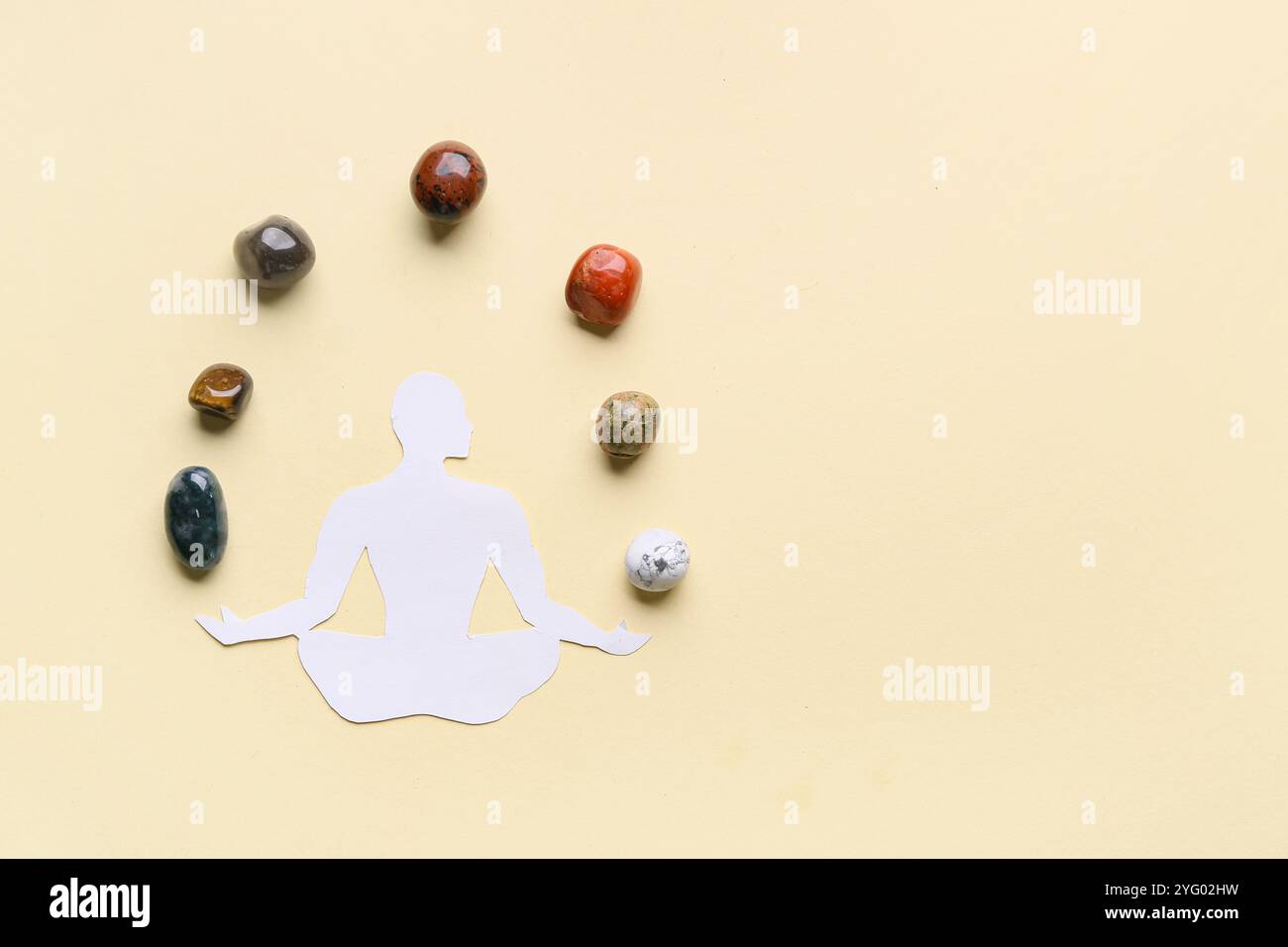 Set of chakra stones and paper figure of meditating human on beige ...