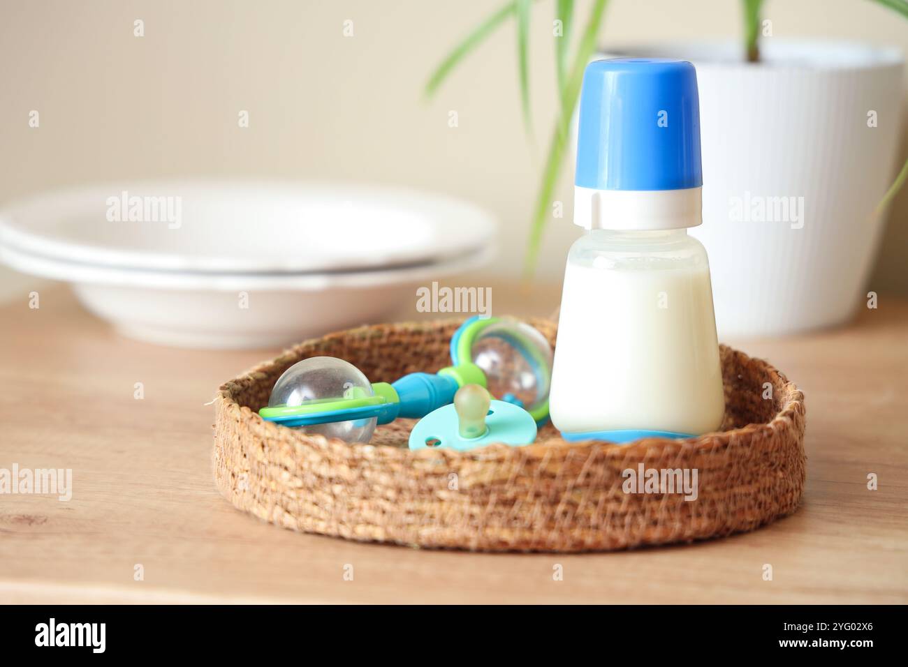 Wicker tray with bottle of baby milk formula, rattle, pacifier and ...