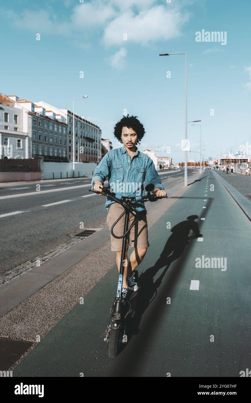 Young man with curly hair riding an electric scooter on an empty urban ...
