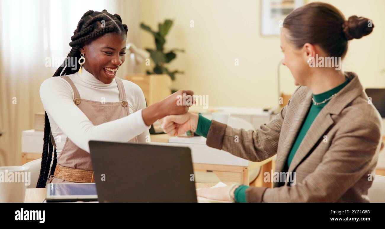 Business women, fist bump and happy in office with success, support and goals by laptop at ...