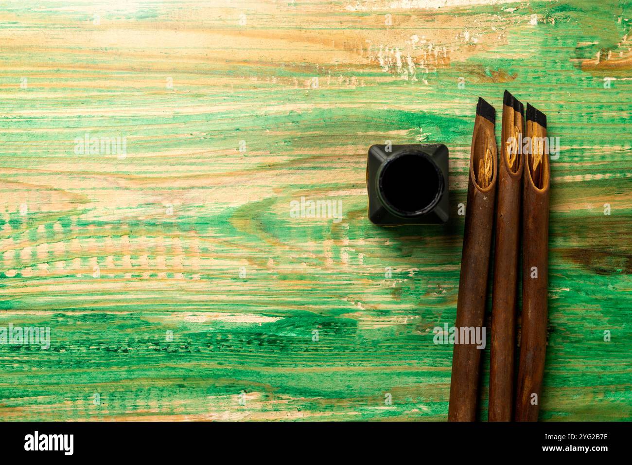 Set of calligraphy reeds covered ink with inkwell on wooden background ...