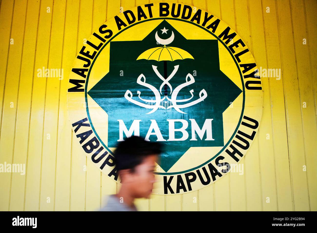 A young man walking past the logo of Majelis Adat Budaya Melayu ...