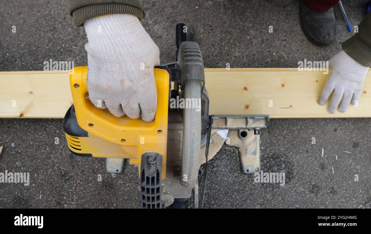 Man in glove holds board with one hand and saws it with hand-held ...