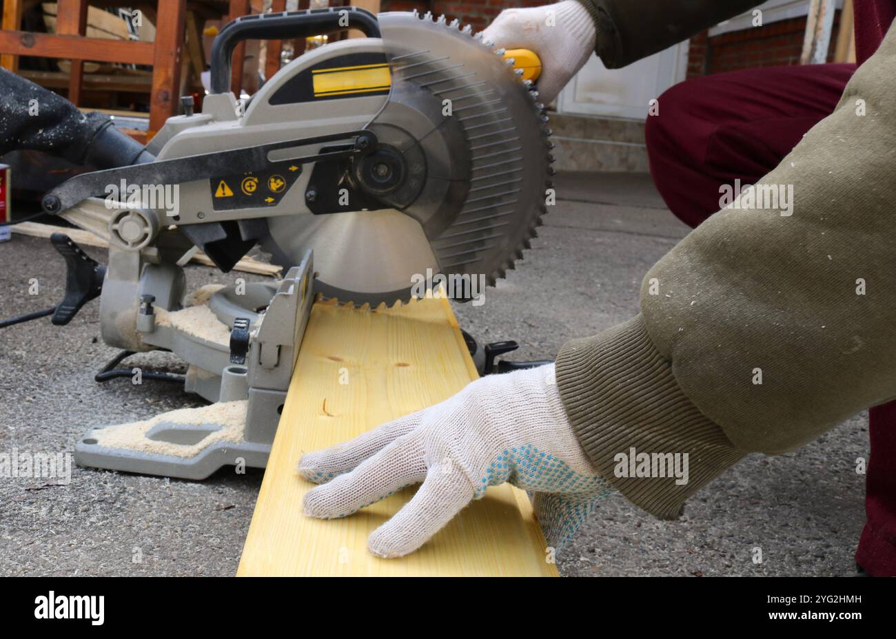 A worker wearing work clothes and construction gloves saws a light ...