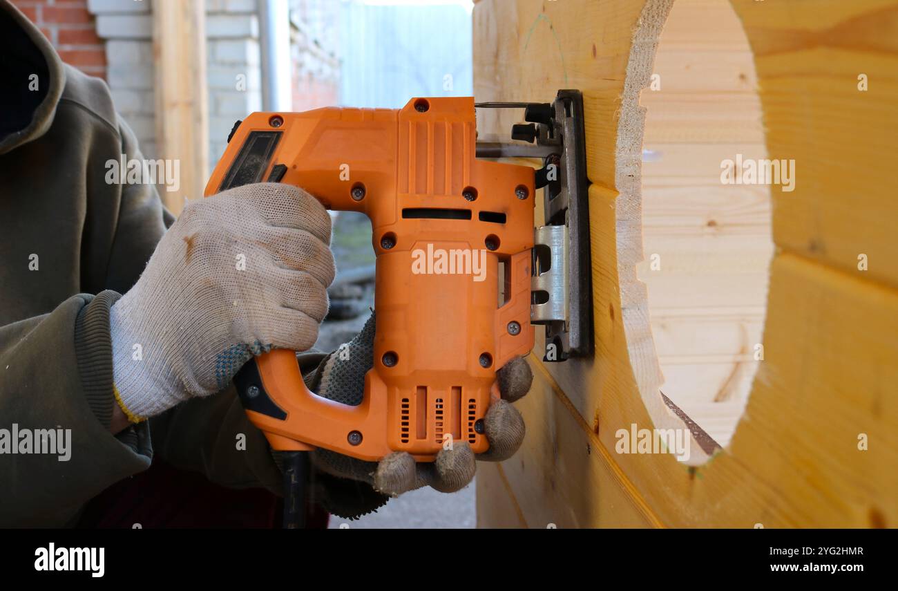 Worker in dirty work gloves cutting a circle in a wooden wall with an ...