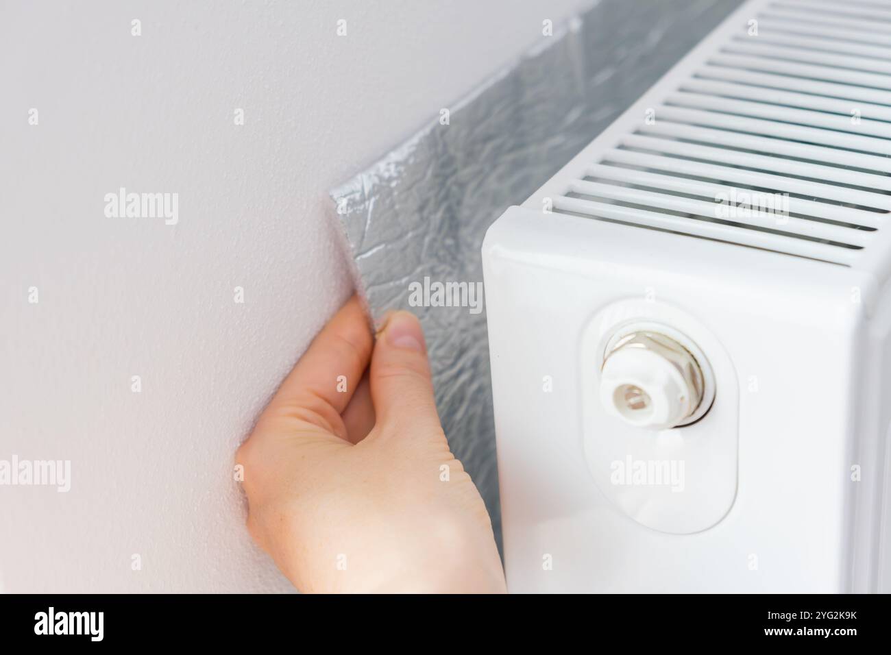 Hand installing thermal insulation behind radiator to reflect heat into ...