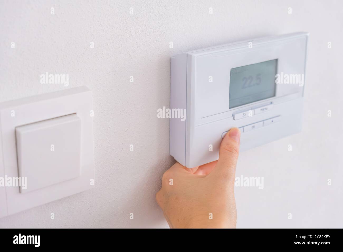 Hand adjusting digital thermostat on wall to control room temperature ...