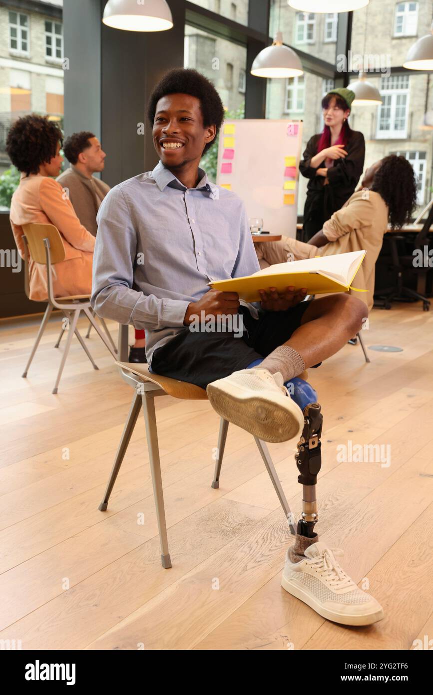 Smiling amputee businessman sitting on chair and looking away ...