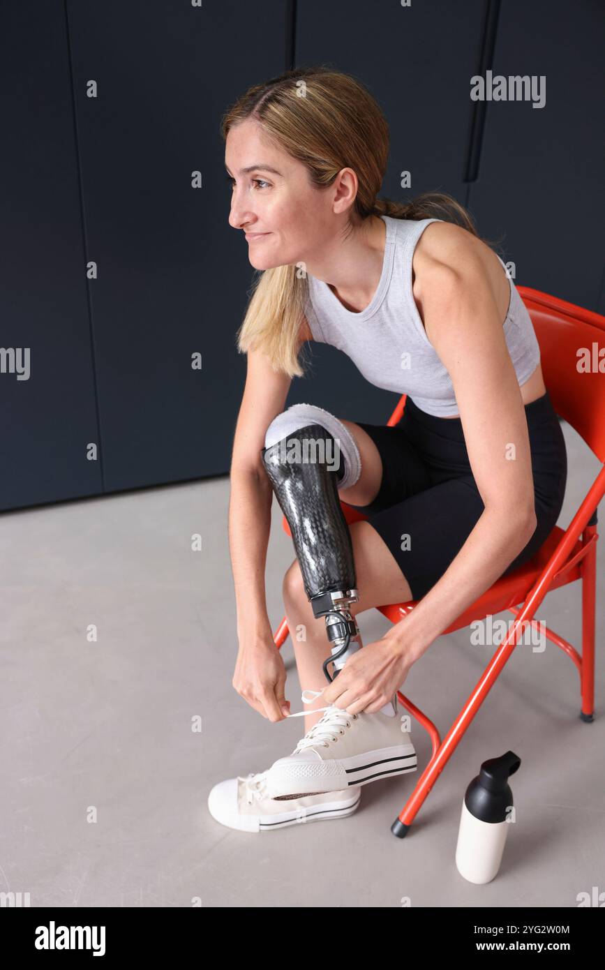 Woman with prosthetic leg sitting on chair and tying shoe in gym Stock ...