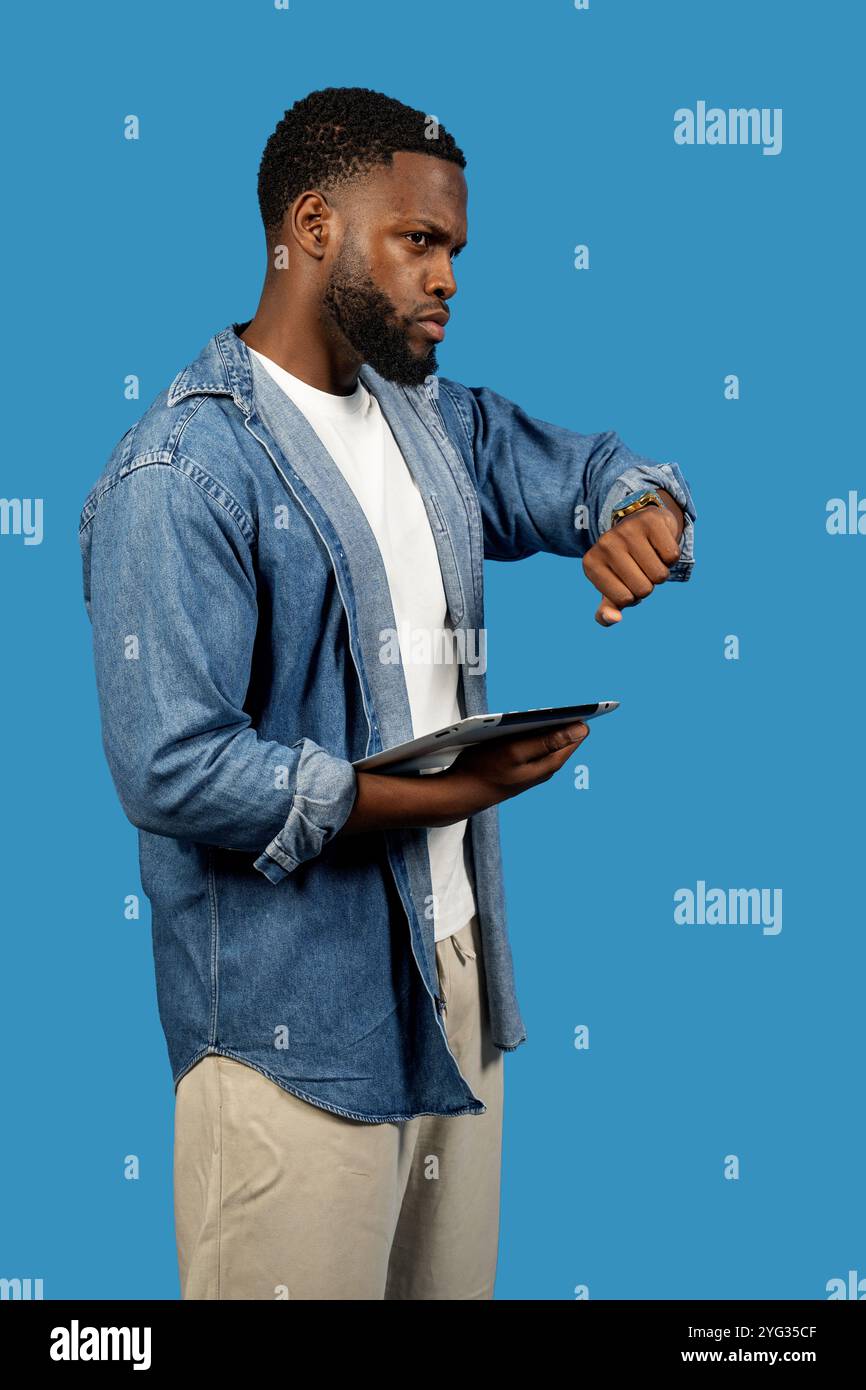 angry black man looking at watch with tablet isolated on blue ...