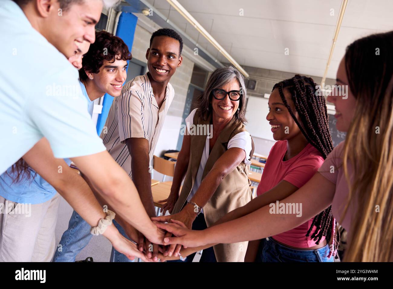 Group of happy multiracial students joining hands with teacher standing ...