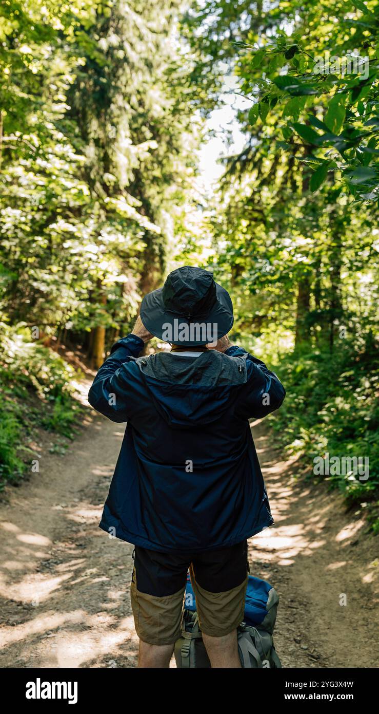 Back view of male in hat and hiking clothes taking photographs during ...
