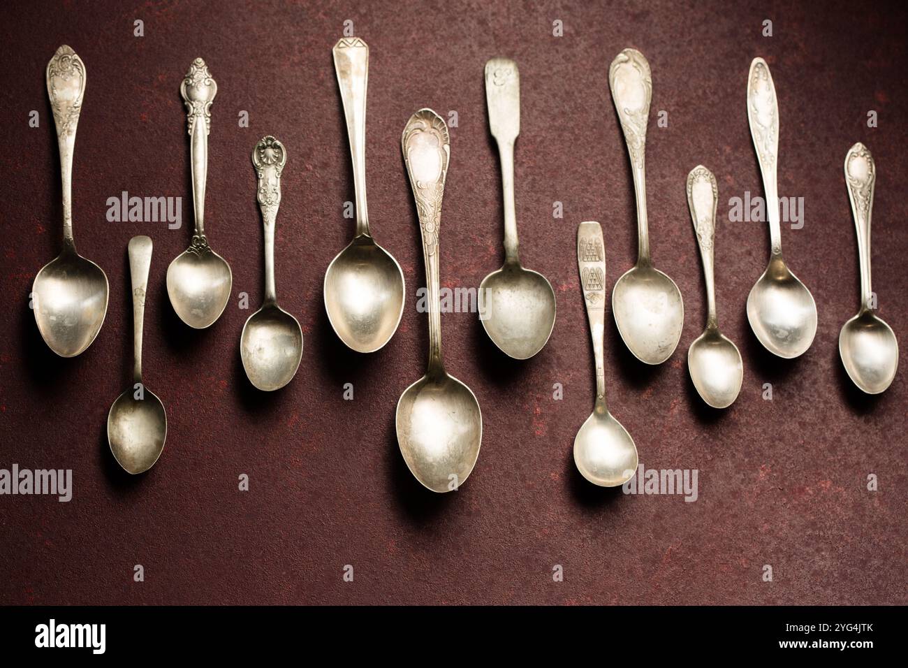 A collection of vintage spoons laid out in rows on a burgundy ...