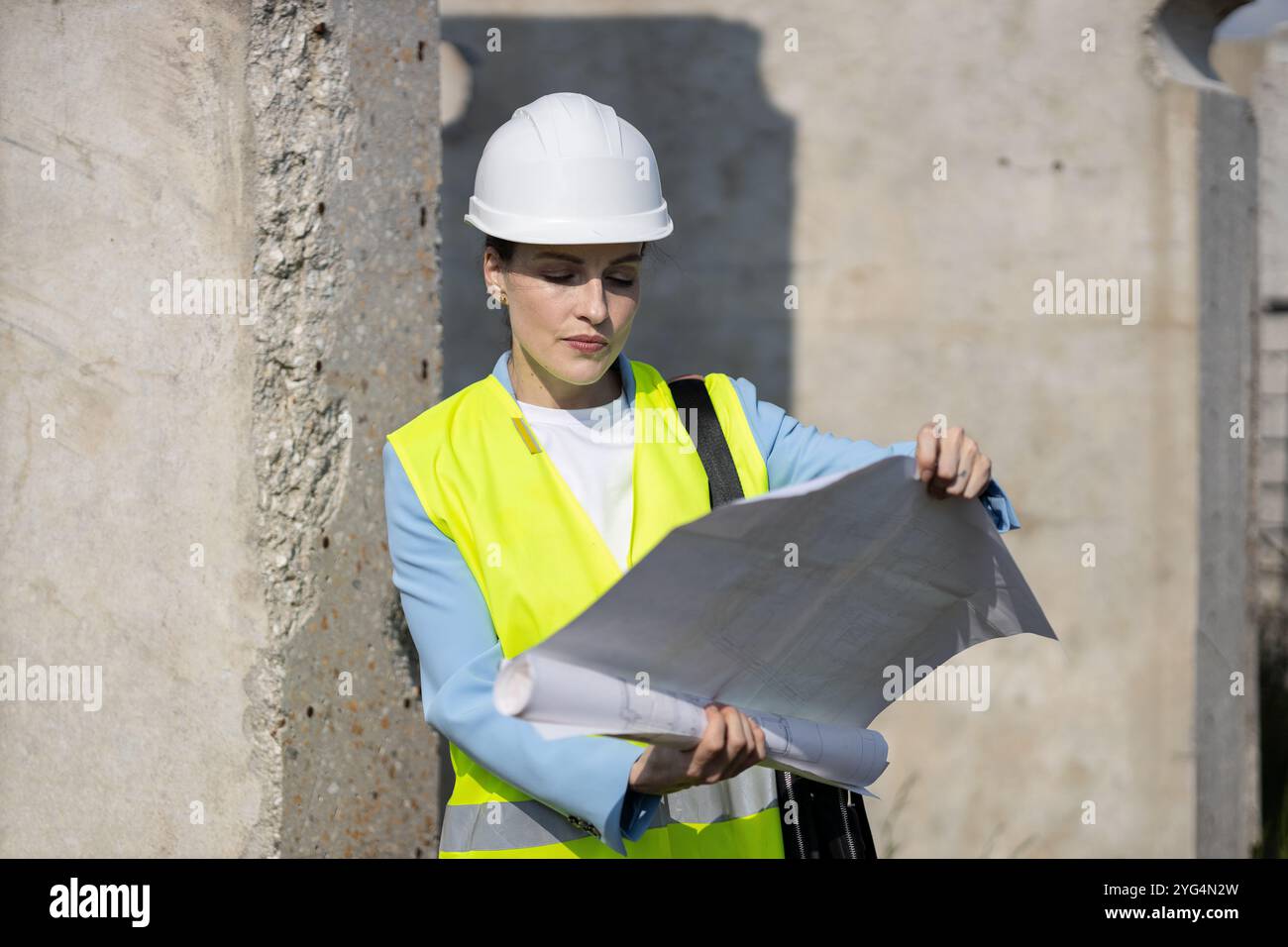 Woman architect wearing safety vest and hard hat reviewing blueprints on a construction site ...