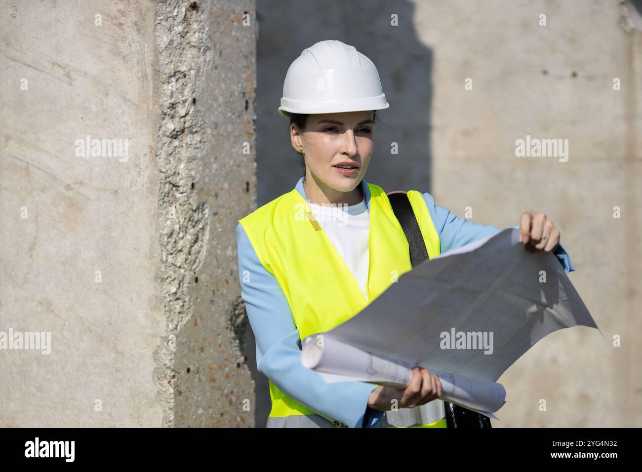 Woman architect wearing safety vest and hard hat reviewing blueprints on a construction site ...