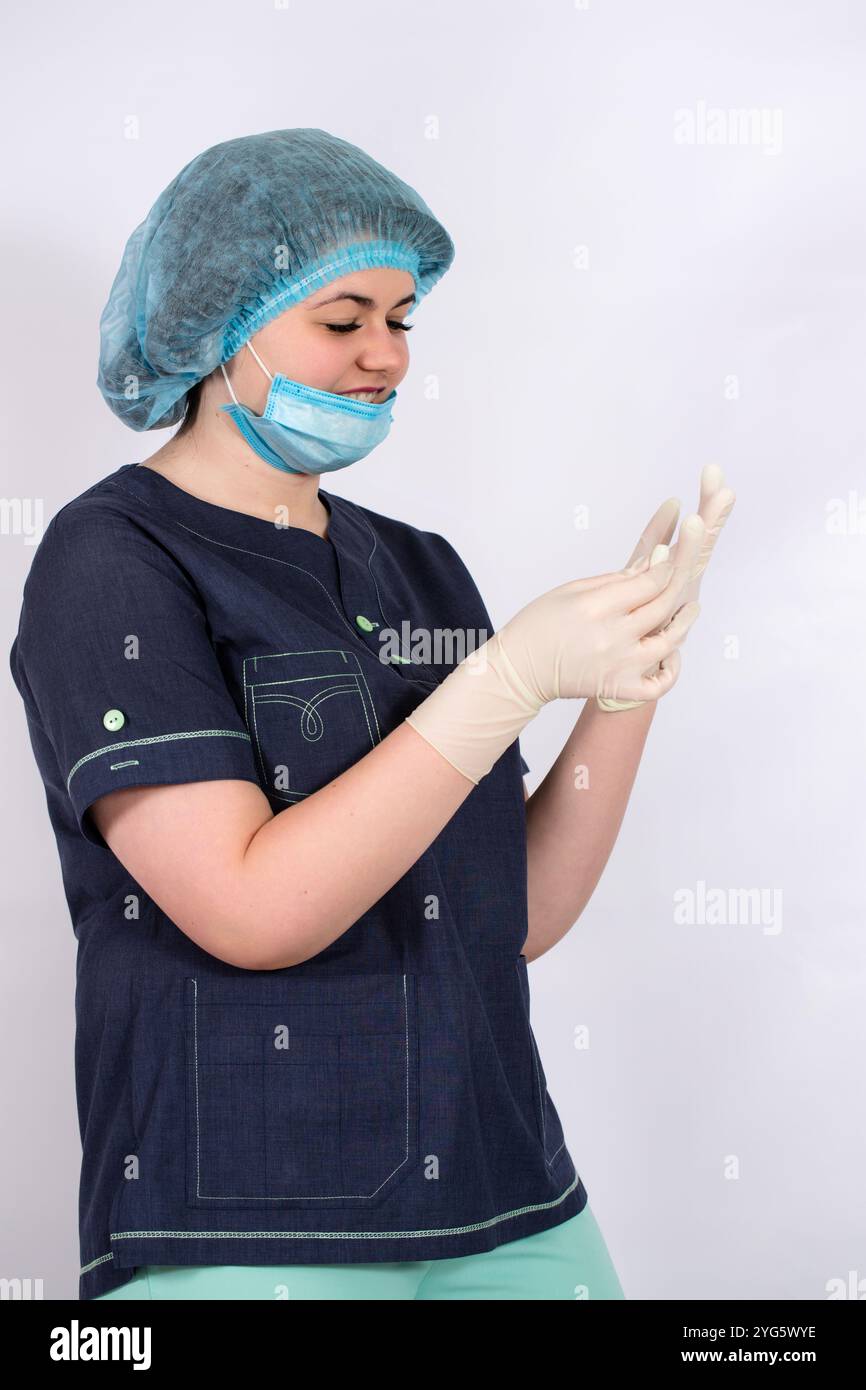 A young nurse in a medical cap and mask is smiling and putting on ...
