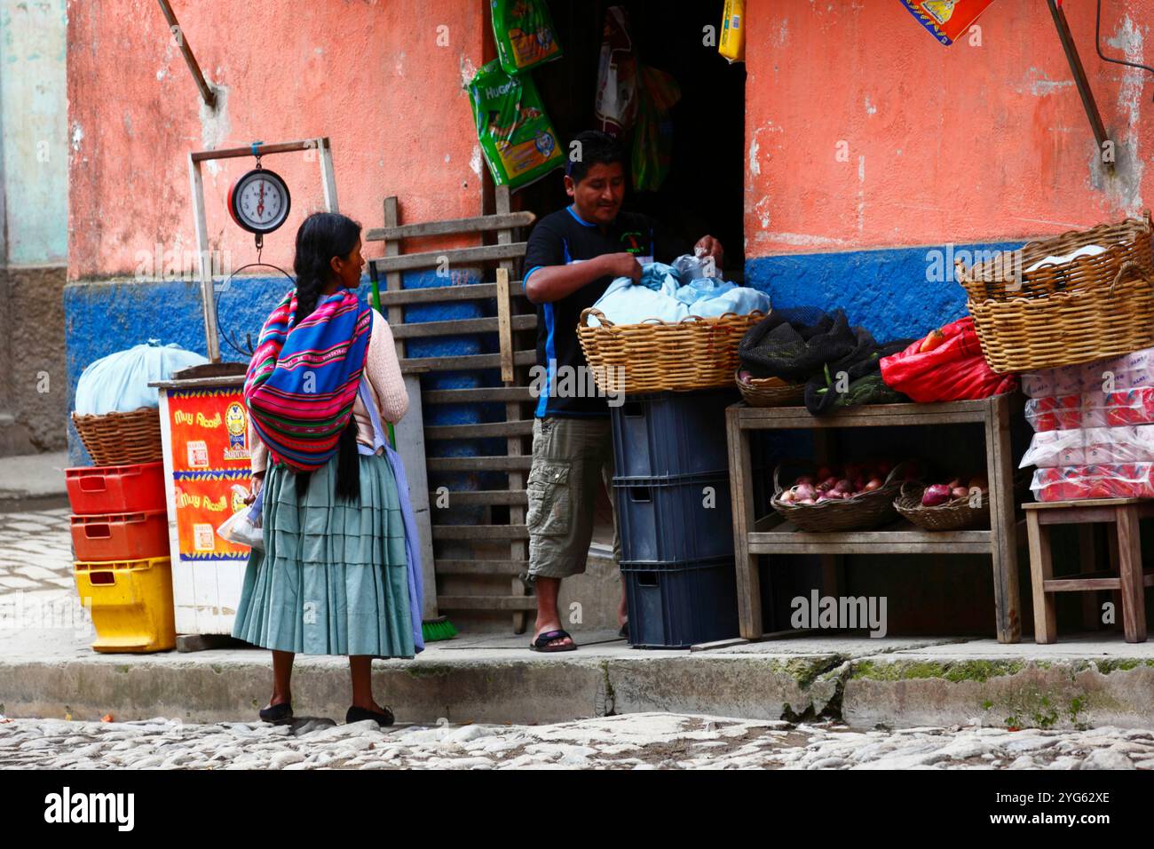 Aymara woman wearing a pollera skirt standing outside a grocery store ...