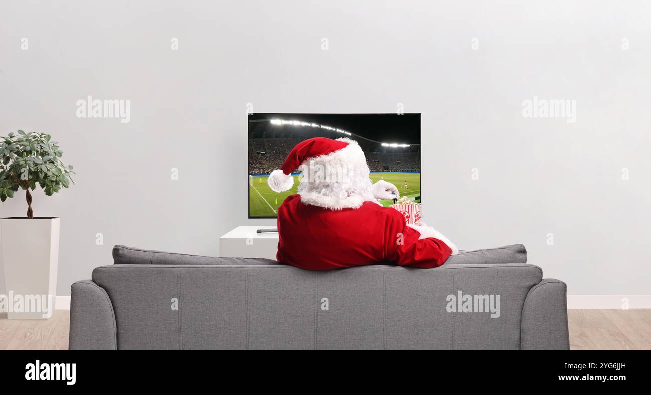 Rear view shot of Santa claus eating popcorn and watching football on ...