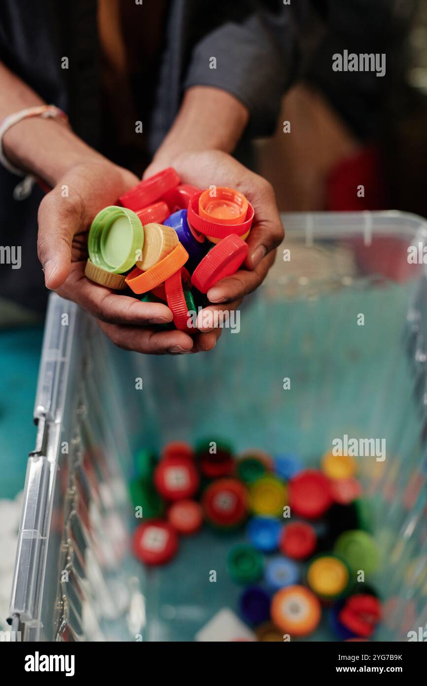 Focus on hands of unrecognizable worker holding red plastic bottle caps ...