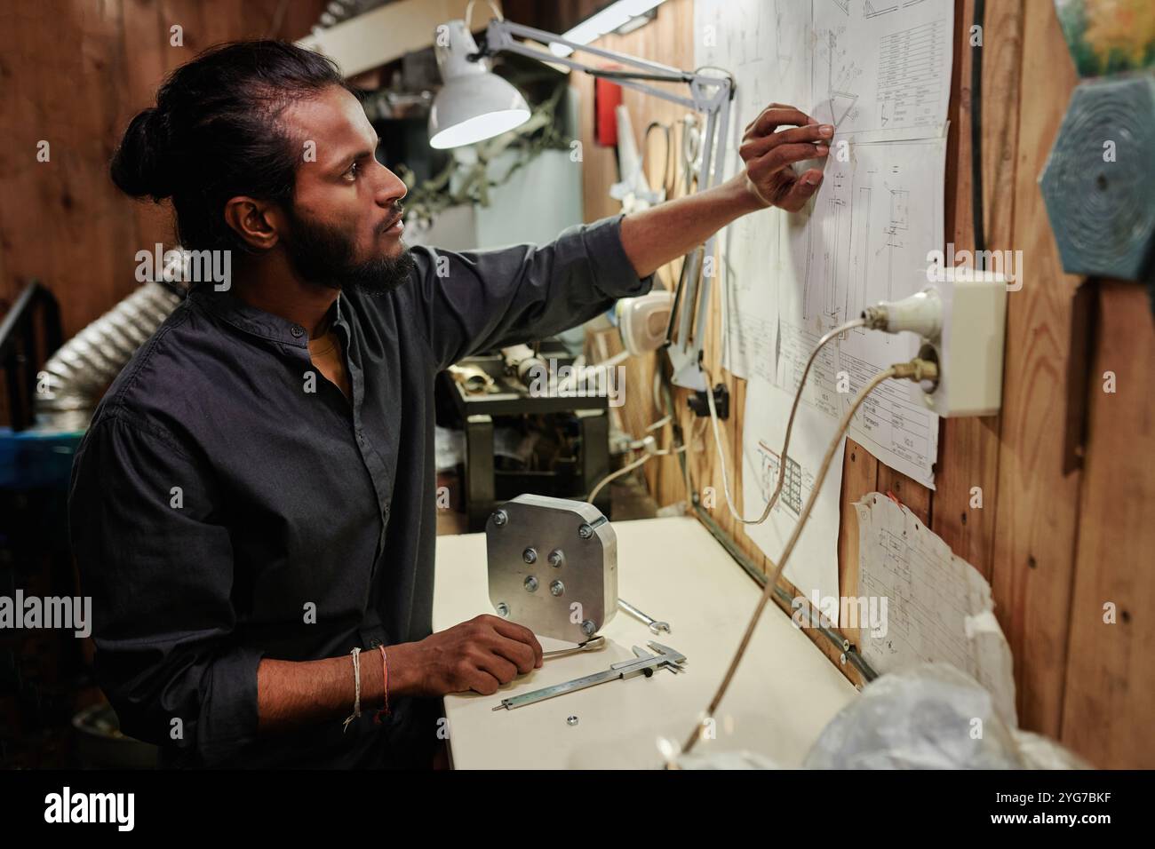 Young technician checking dimensions of detail on technical drawings ...
