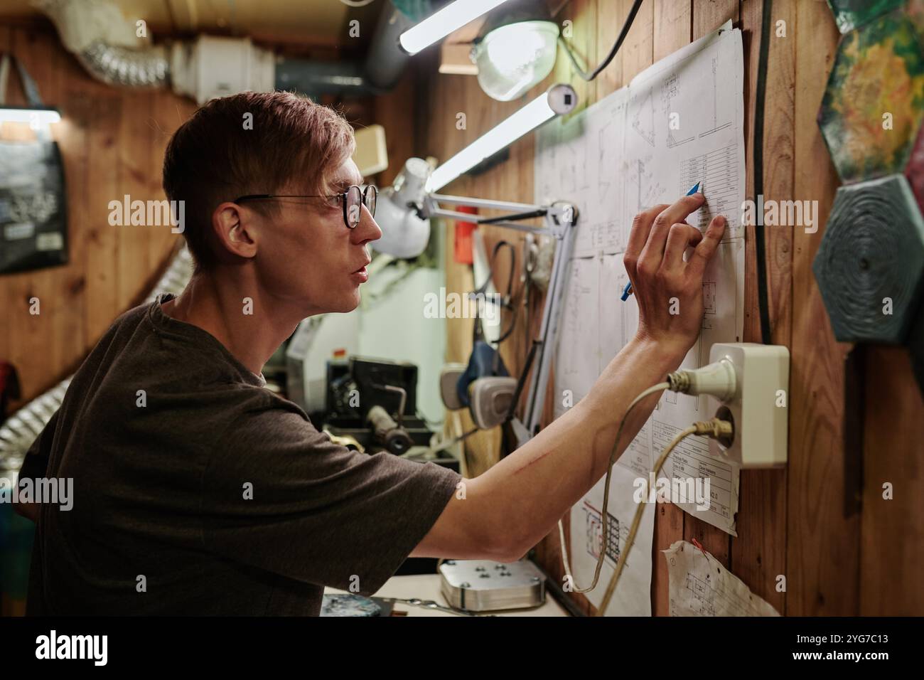 Side view of young engineer with pen checking dimensions on technical ...