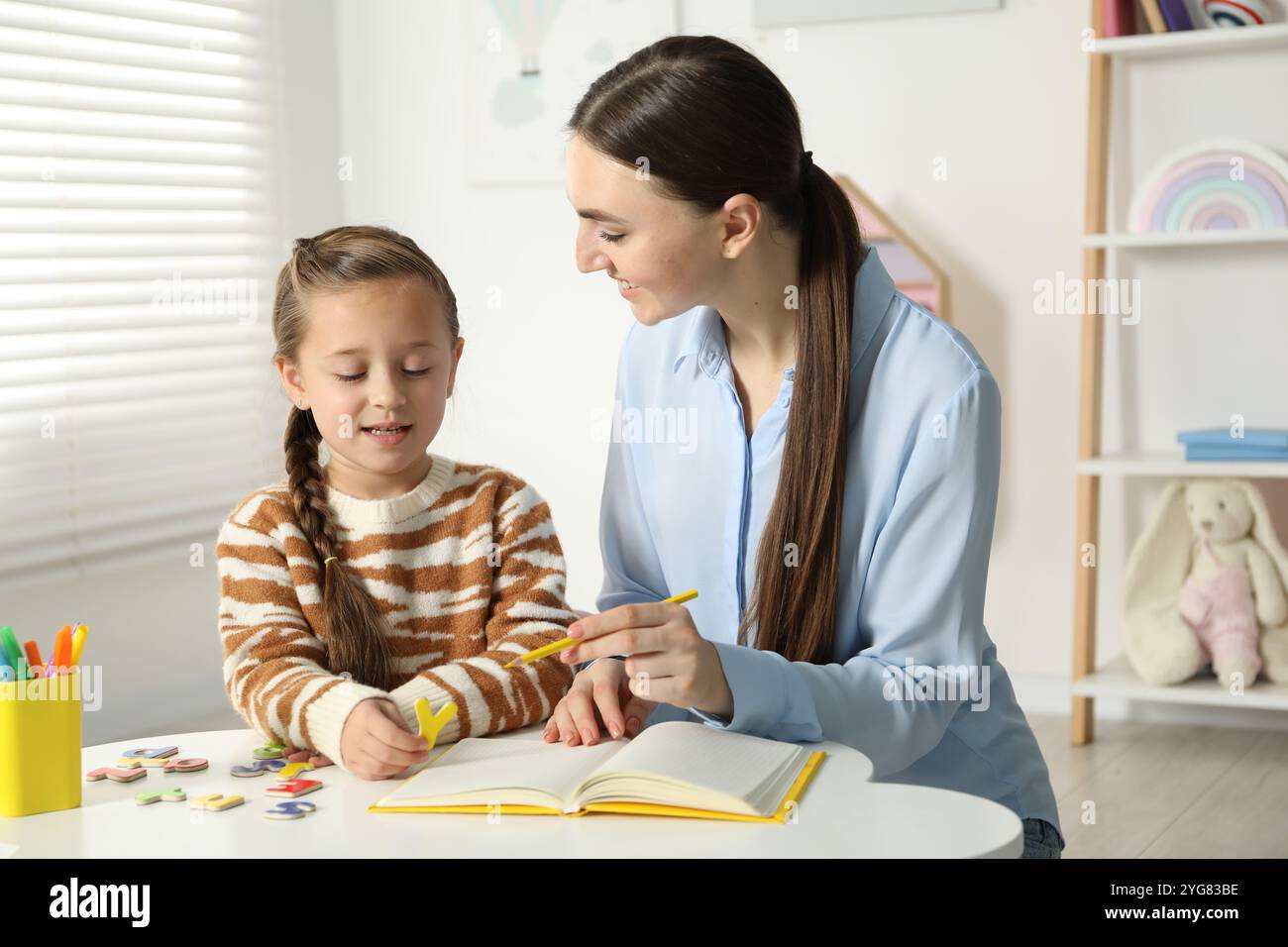 Speech therapist teaching little girl alphabet with magnetic letters at ...