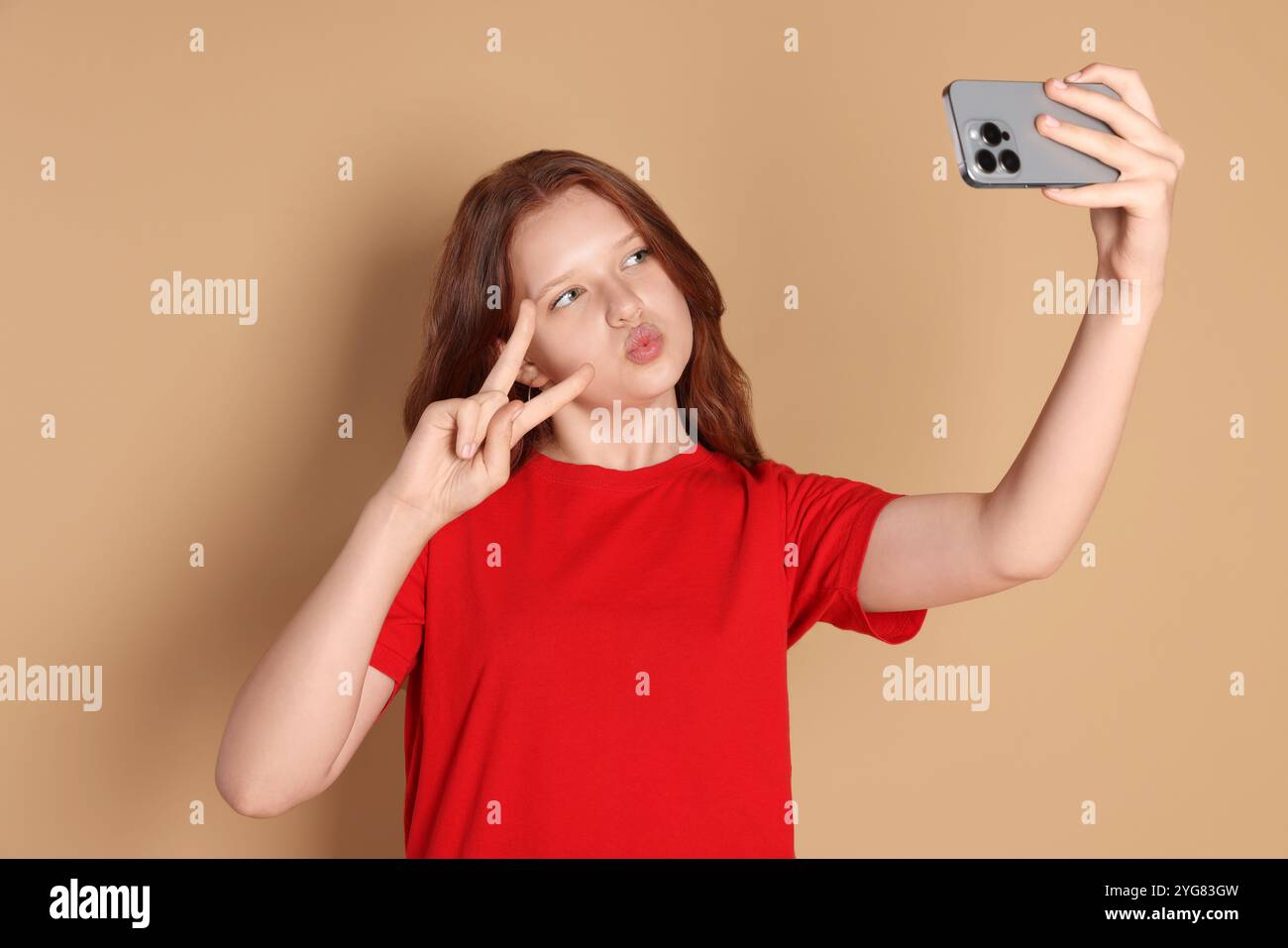Cute teenage girl taking selfie and showing peace sign on beige ...