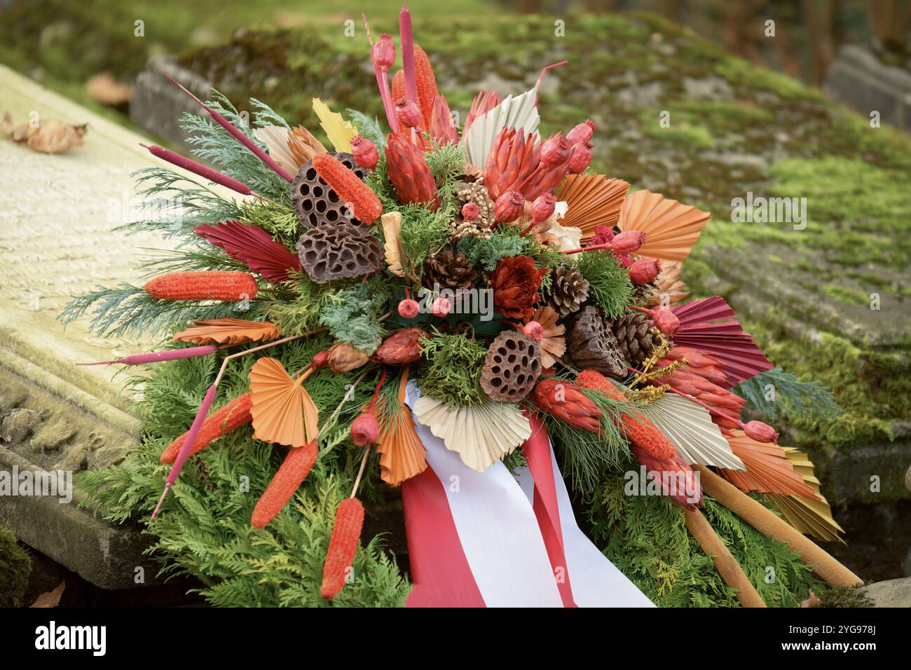 an autumnal funeral arrangement with a red and white ribbon on a ...