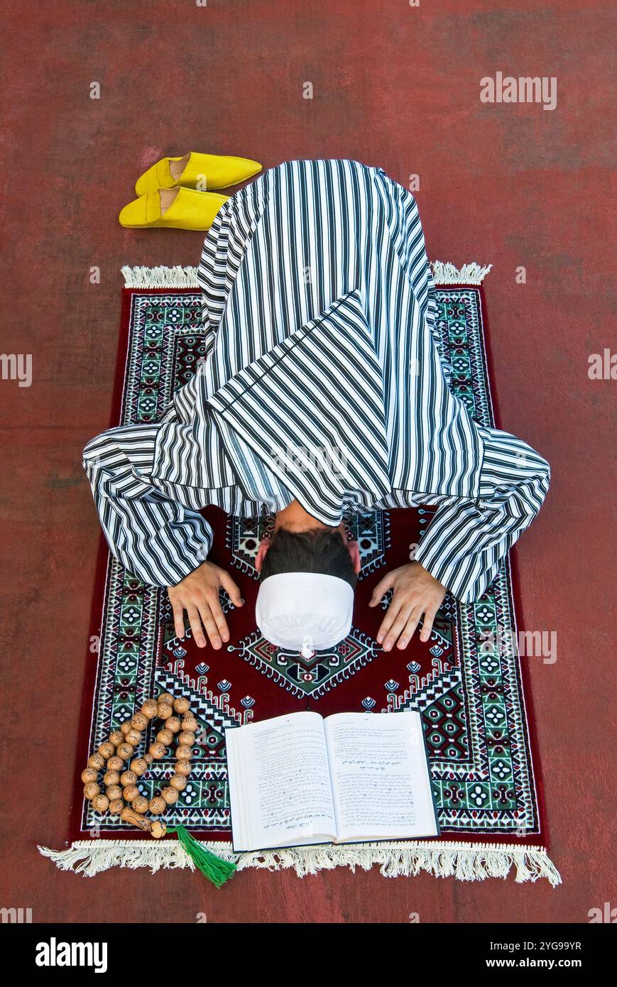 Muslim man prostrating himself on a prayer carpet, his shoes beside him ...