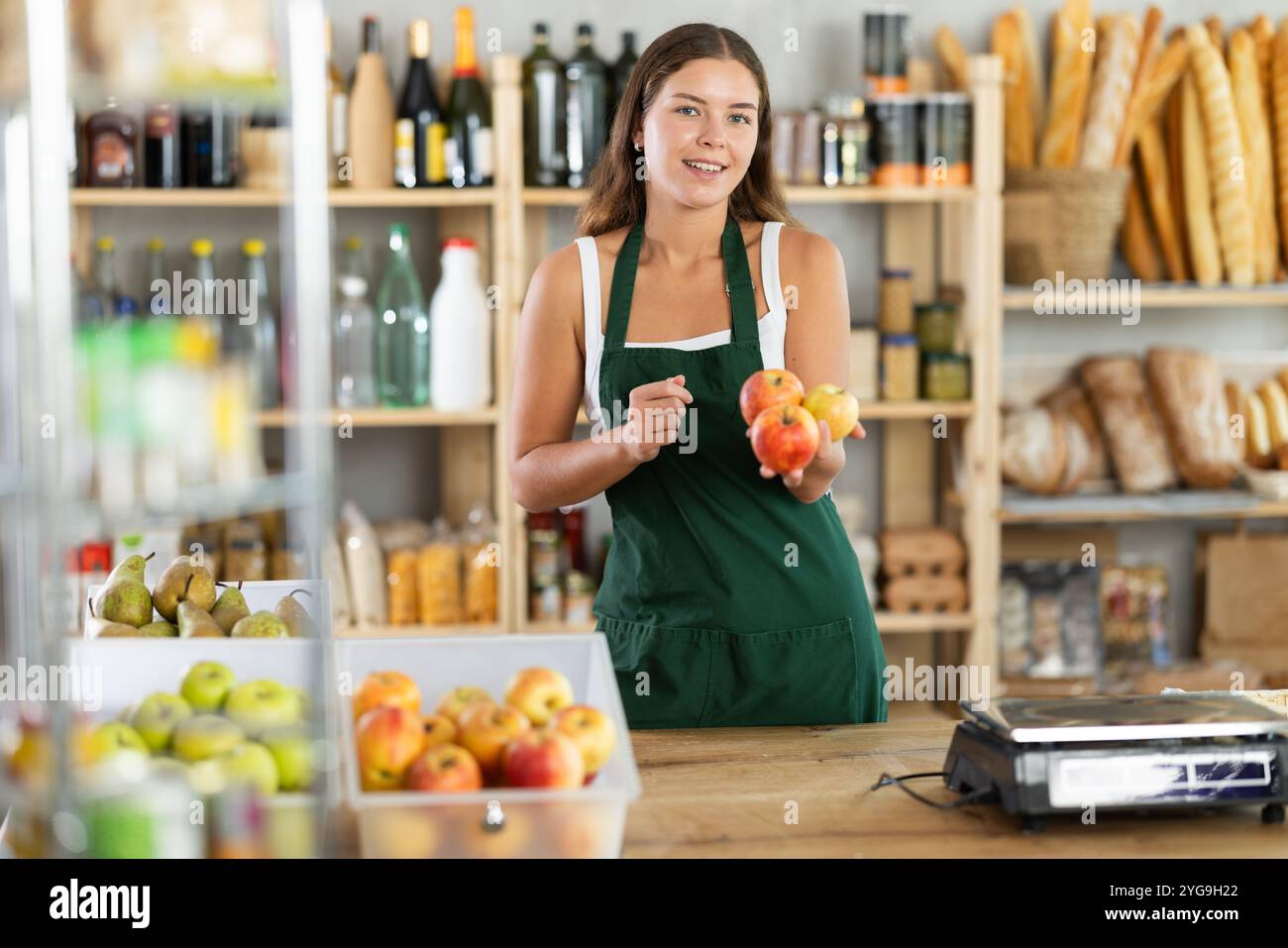 Young woman seller offering apples in grocery store Stock Photo - Alamy